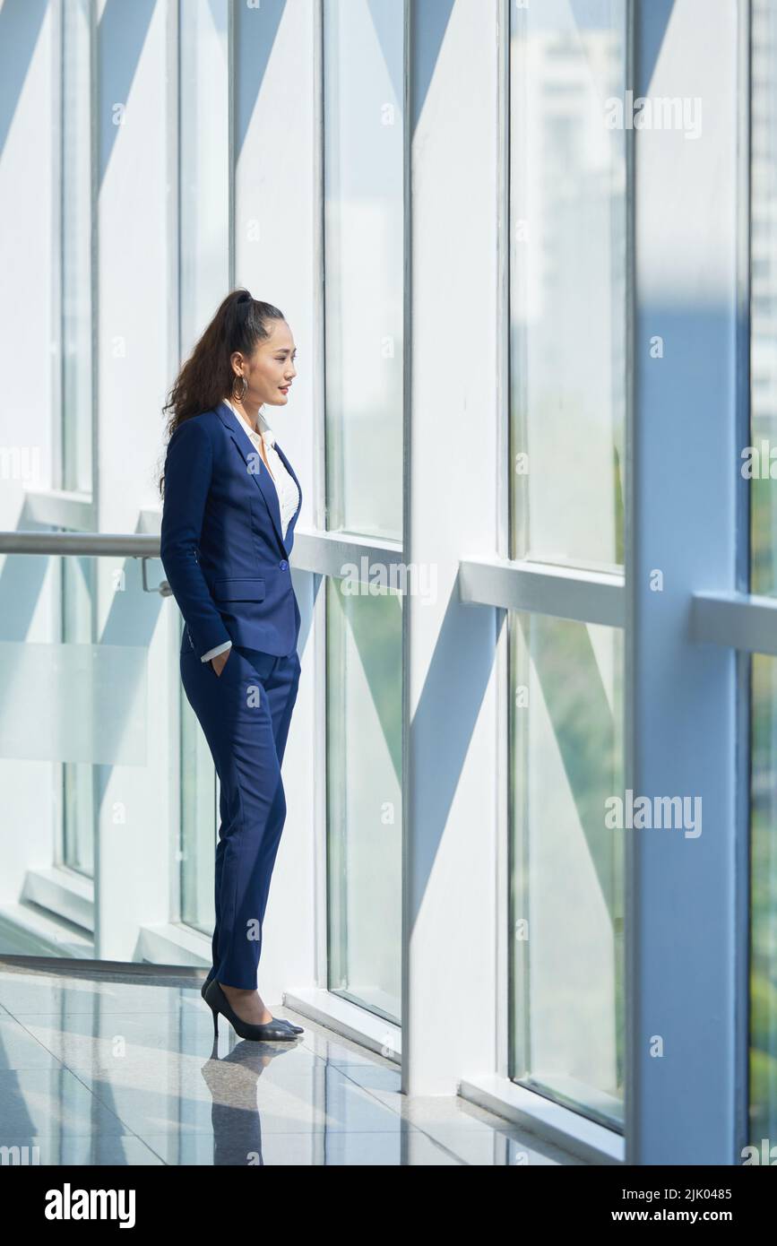 Smiling pensive young business lady looking through office window Stock ...