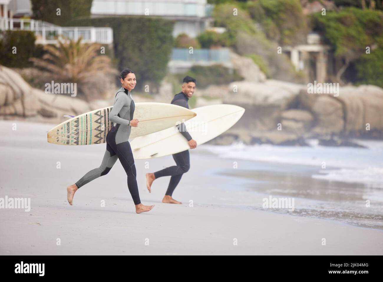 Lets go surfing. a young couple running into the water with surfboards ...