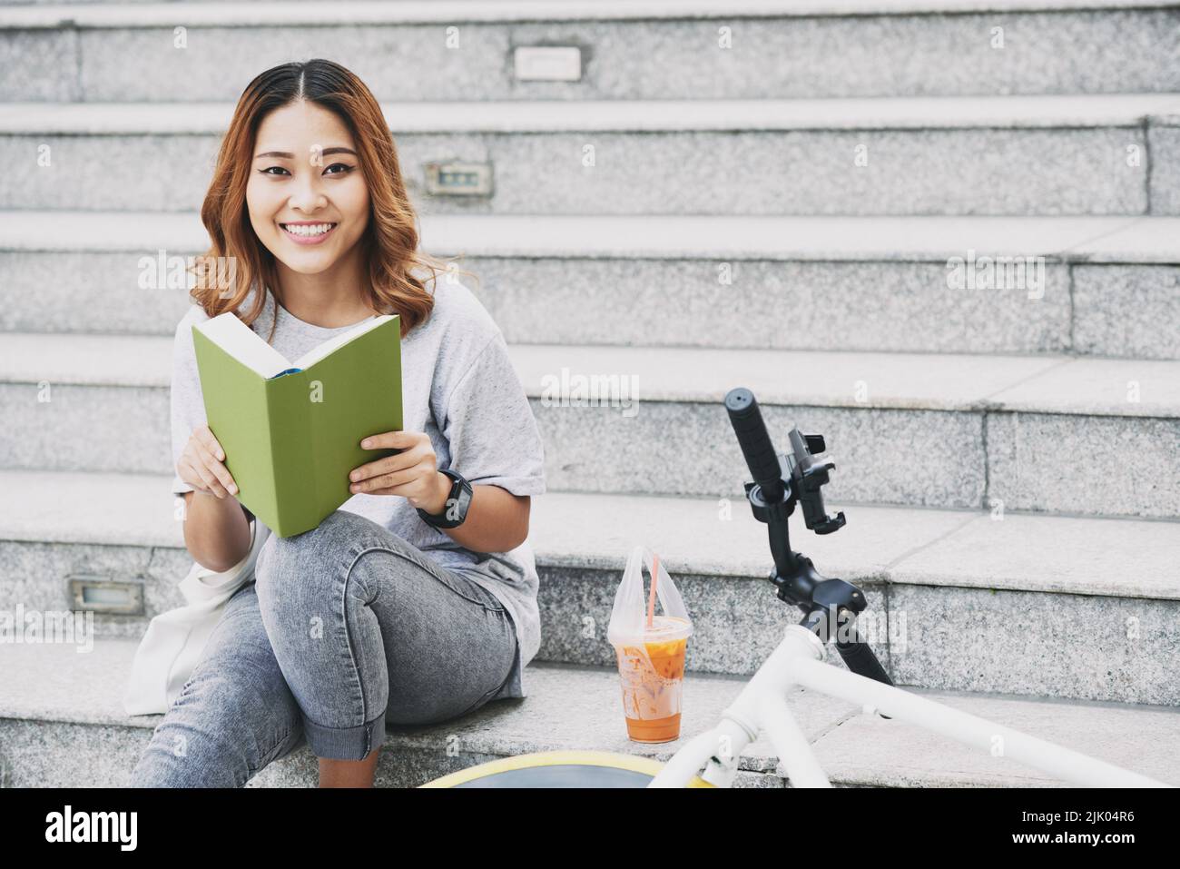 Portrait of pretty Vietnamese student with a book sitting on stairs ...