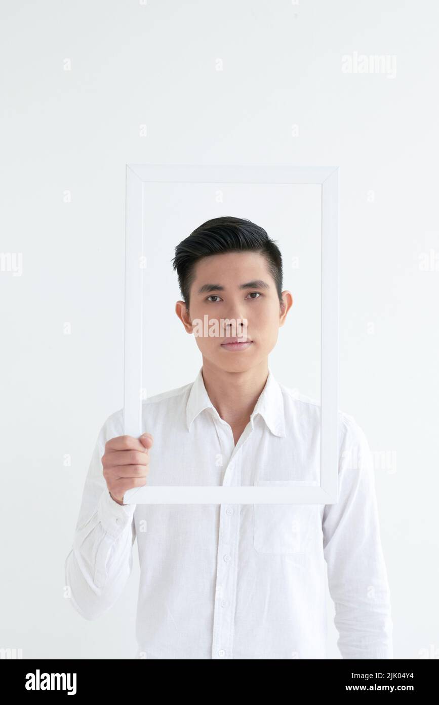 Young unsmiling Asian man looking at camera through picture frame Stock ...