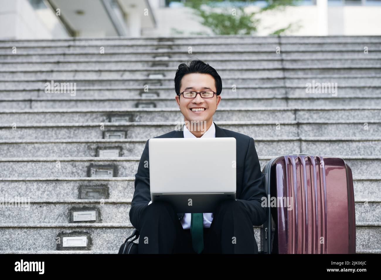 Happy Vietnamese businessman sitting on stairs and working on laptop ...
