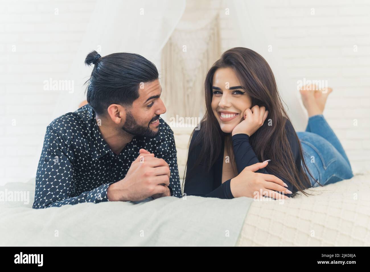 Young white couple relaxing in bedroom together. Boyfriend looking at ...
