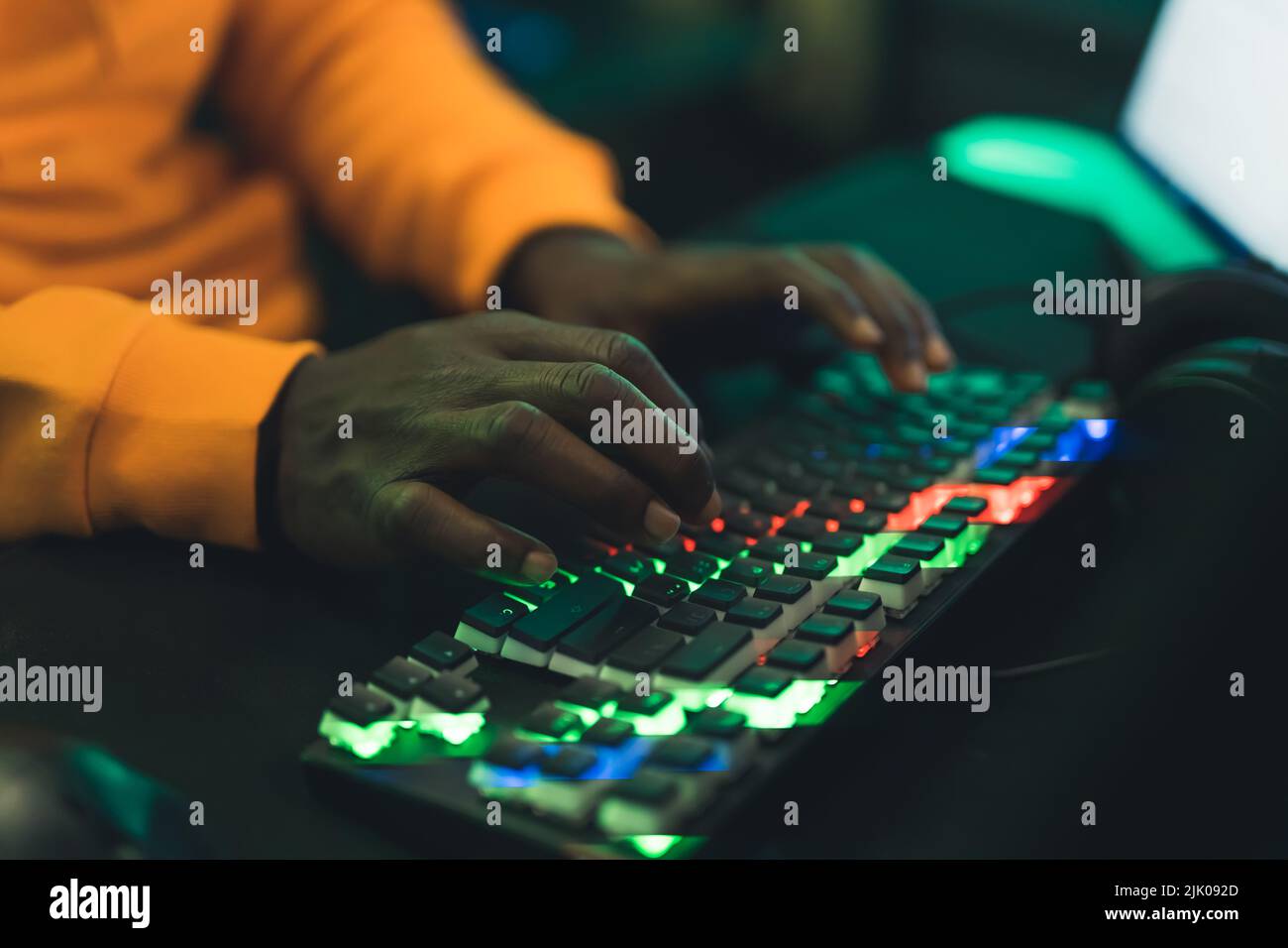 Black man in orange sweatshirt typing on rainbow-colored professional ...