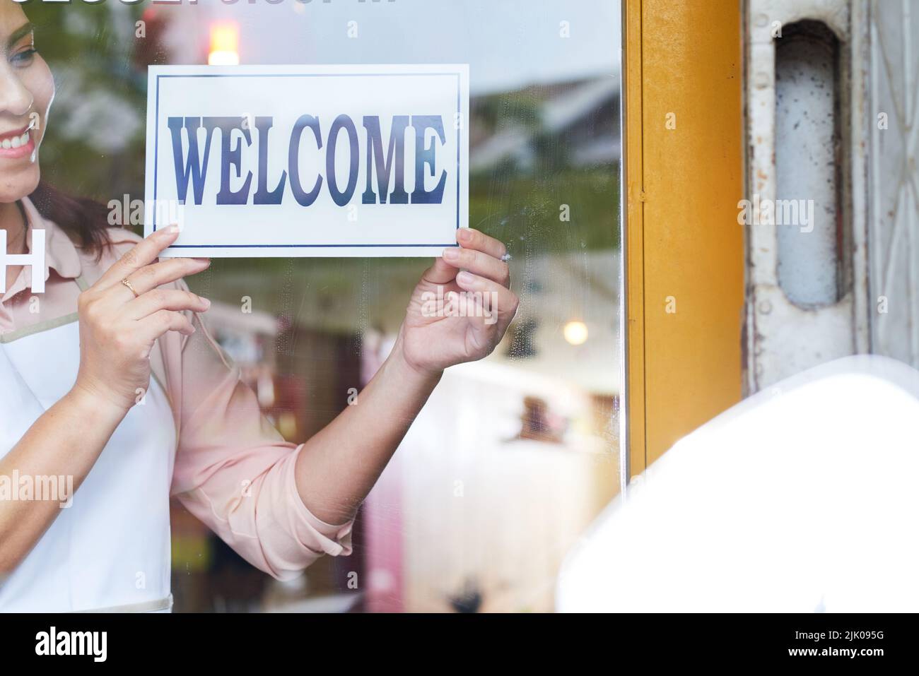 Cheerful young Vietnamese shop owner turning welcome sign on the glass ...