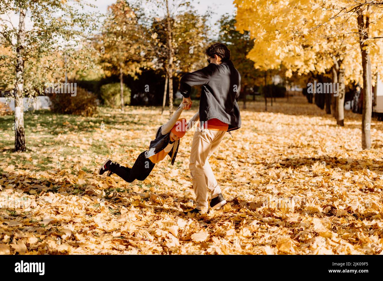 Father and son having fun in autumn park with fallen leaves, throwing up leaf. Child kid boy and ...