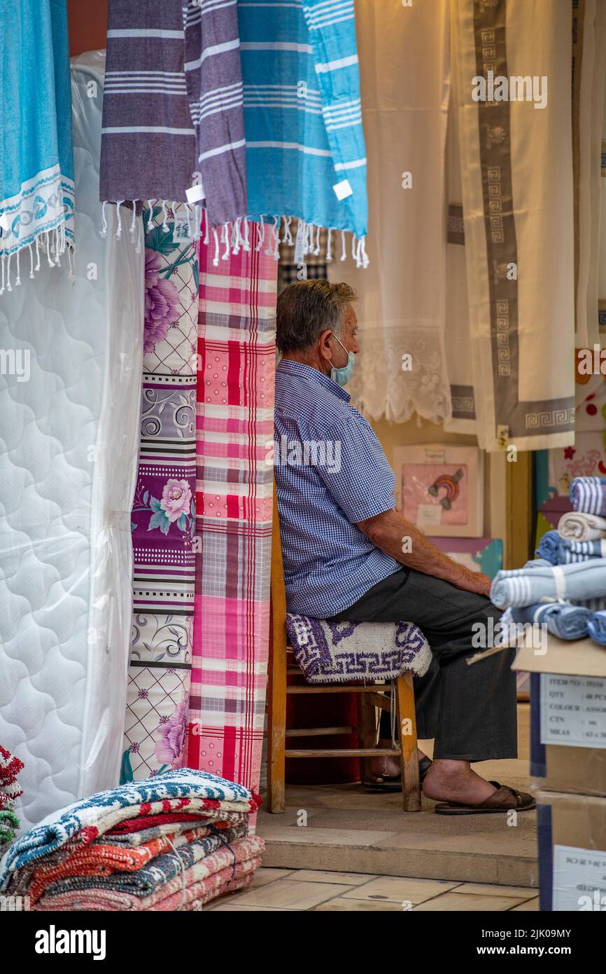 greek shop owner relaxing on a chair at linen traditional gift shop on ...