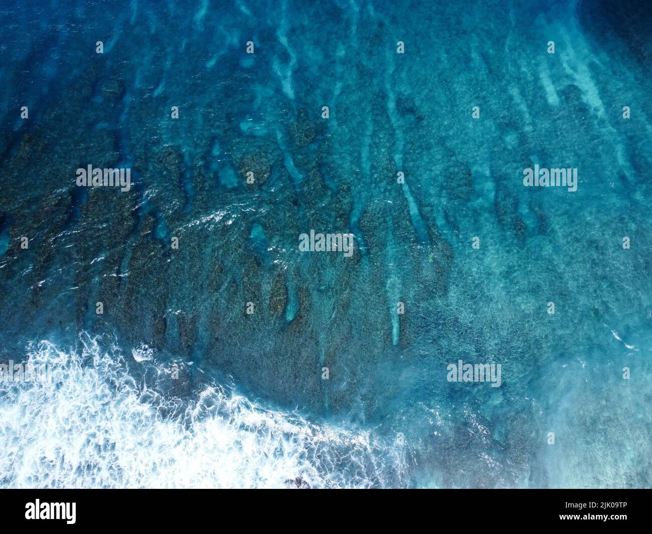Aerial down shot of crystal clear water and white waves crashing agaist ...