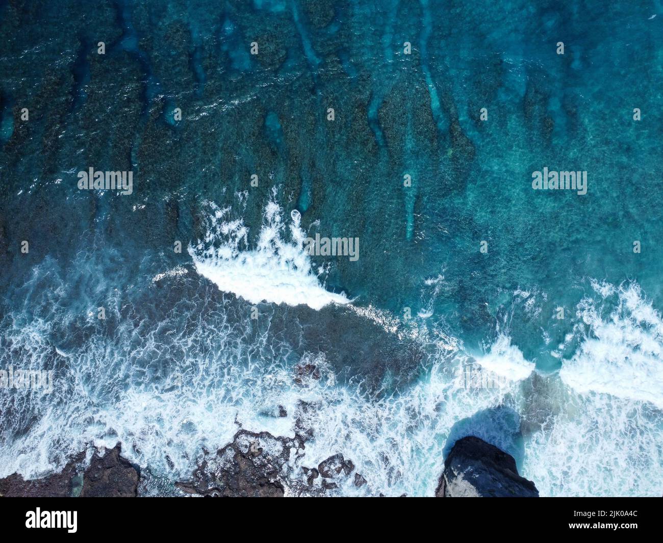 Aerial down shot of crystal clear water and white waves crashing agaist ...