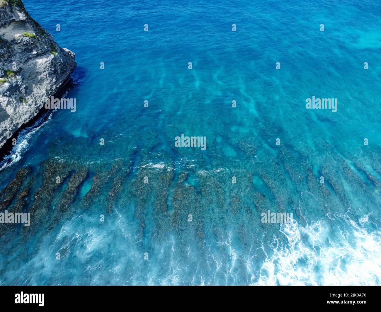 Aerial down shot of crystal clear water and white waves crashing agaist ...