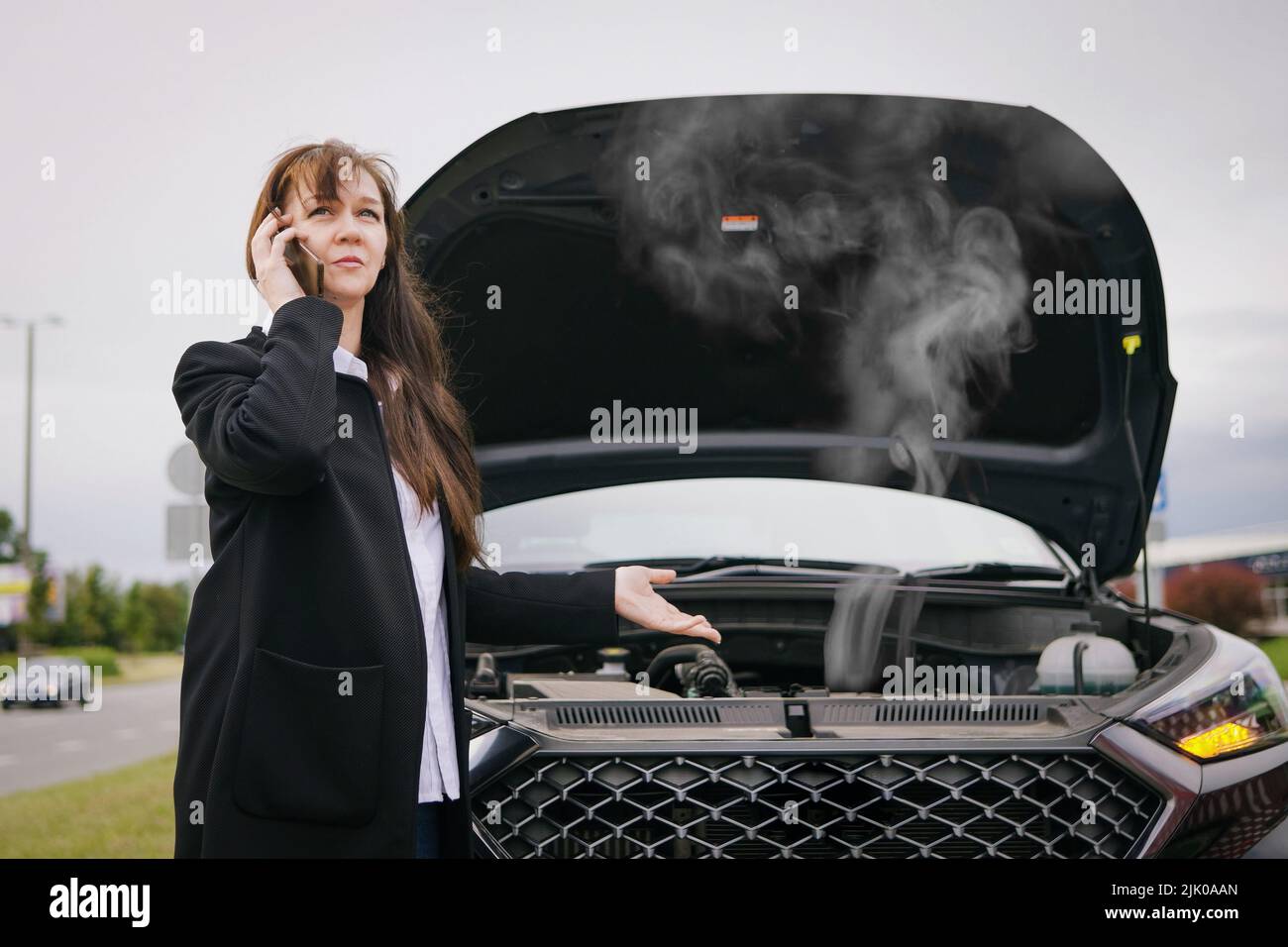 a woman next to a smoking car calls for help. a woman is talking on the ...