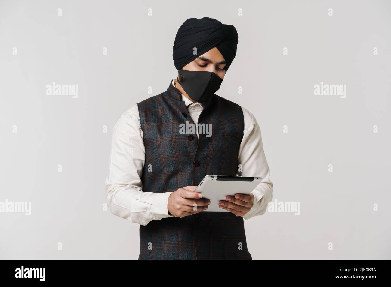 South asian man wearing turban and face mask using tablet computer ...
