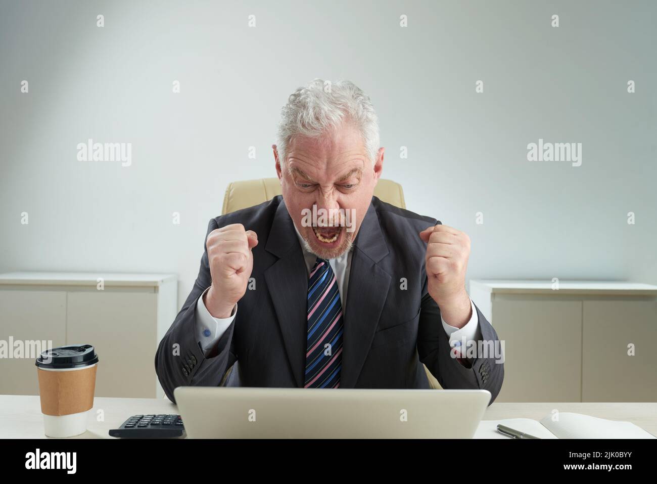 Angry senior businessman wearing classical suit holding hands in fists ...