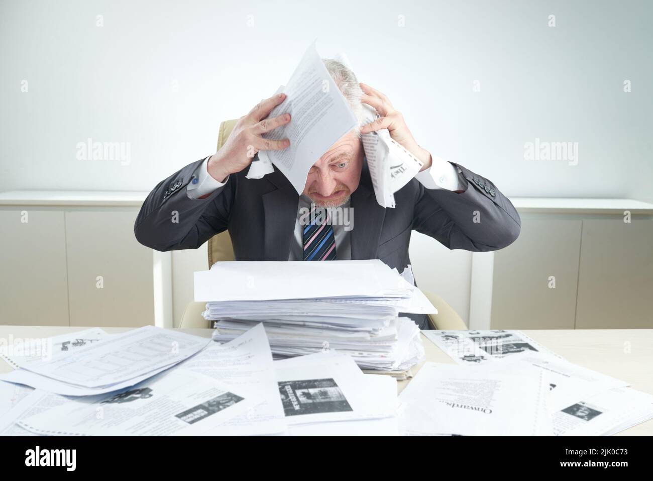 Angry senior businessman covering his head with documents while sitting ...