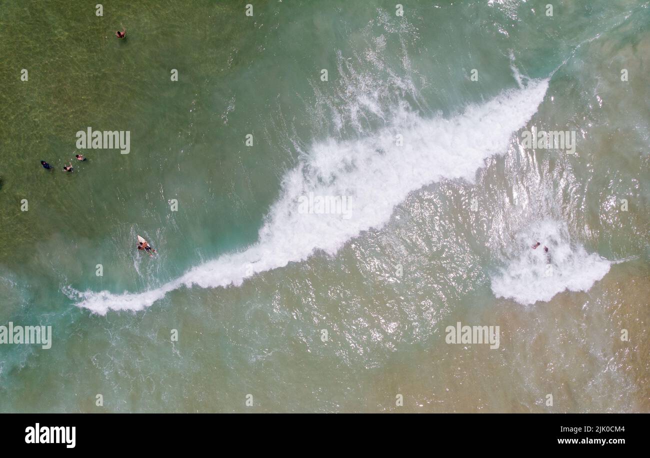 An aerial view of people swimming and surfing in the sea near the sandy ...