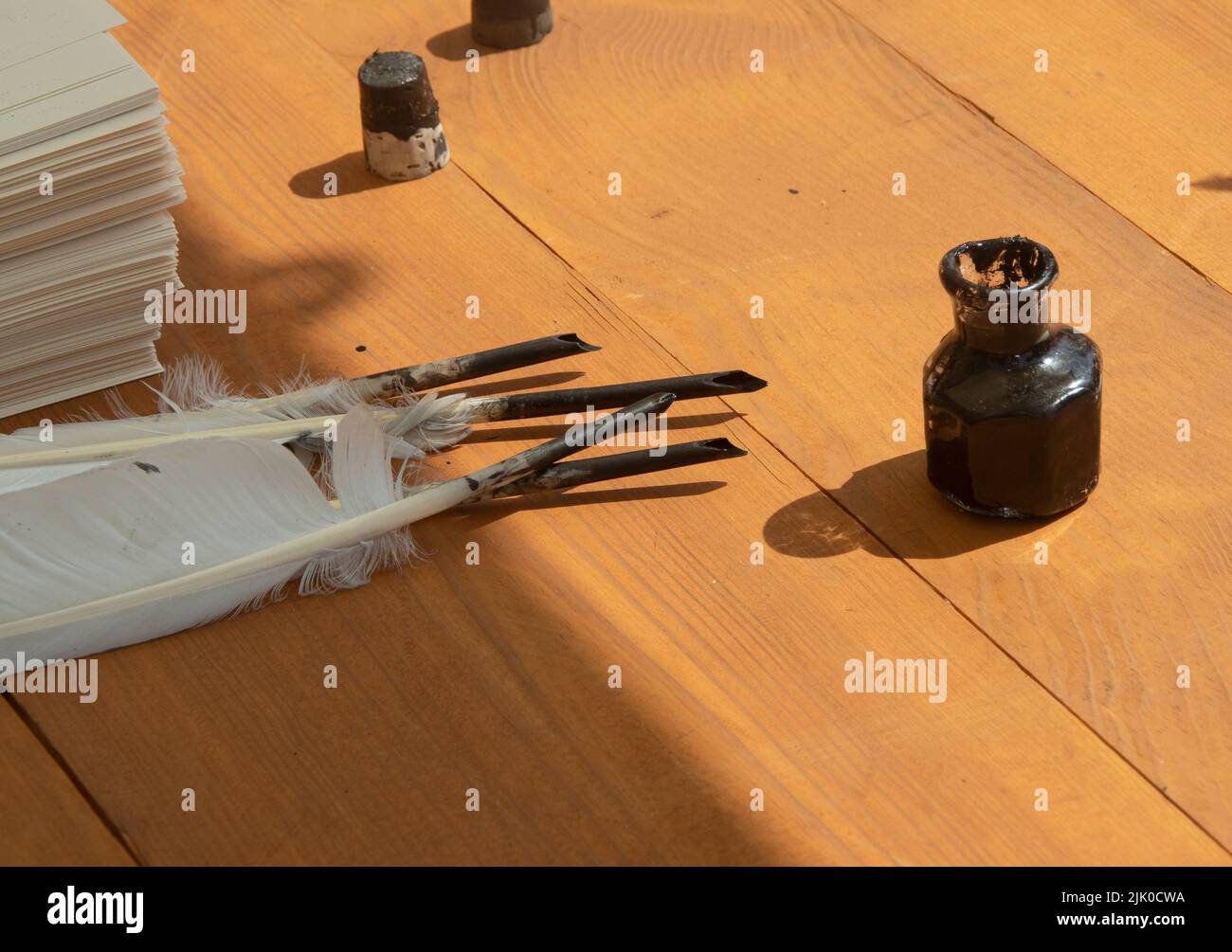 A stack of quill pens, paper and inkwell on wooden table ready for ...