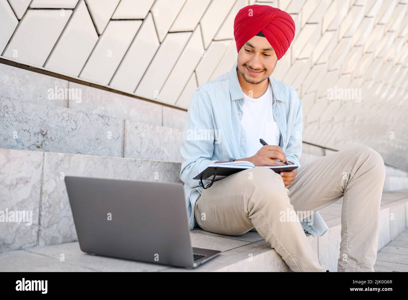 Indian student man in traditional turban sitting outdoors and using ...