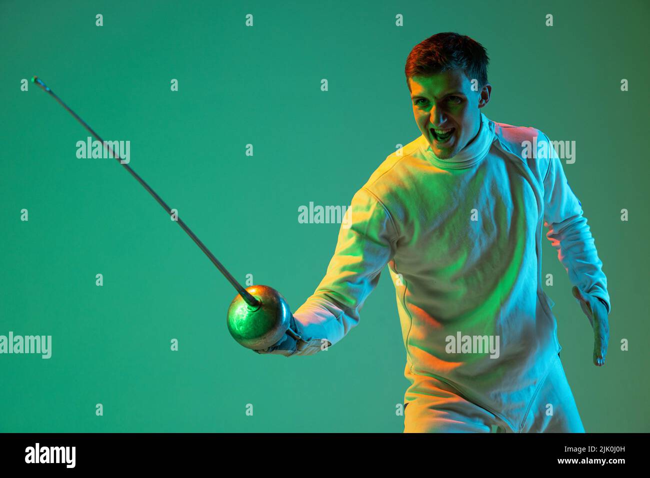 Studio shot of young man, fencer with smallsword practicing fencing ...