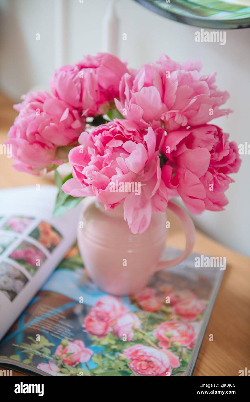 A vertical shot of beautiful pink peonies in a vase on top of an open ...