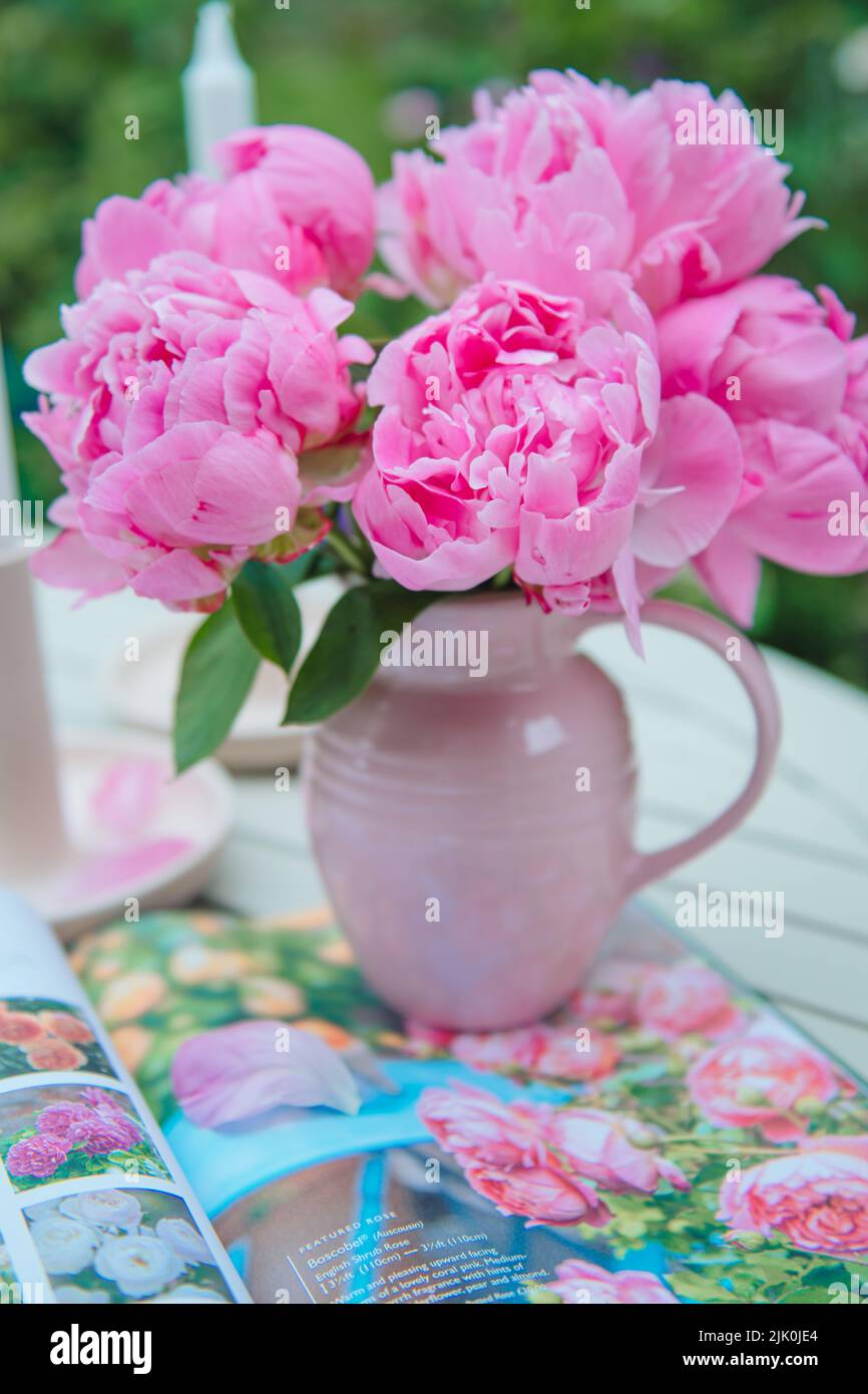 A vertical shot of beautiful pink peonies in a vase on top of an open ...