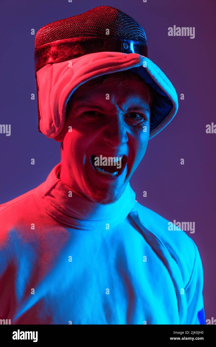 Portrait of young tall male fencer in fencing costume and mask holding ...