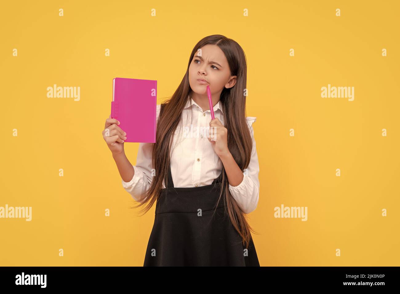 Thoughtful child think holding school book and pen yellow background ...