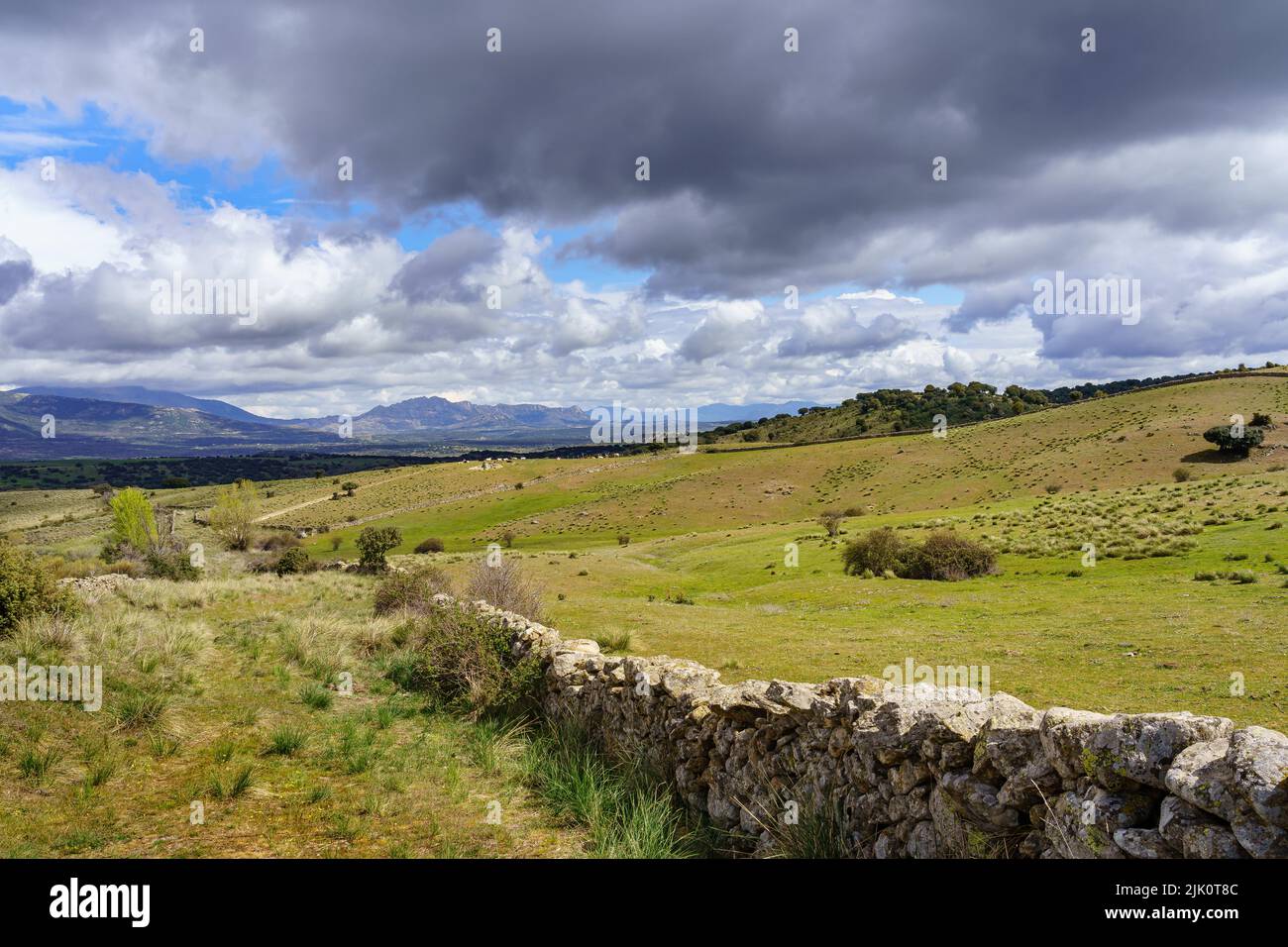 Green landscape with dramatic sky and natural stone fence separating ...