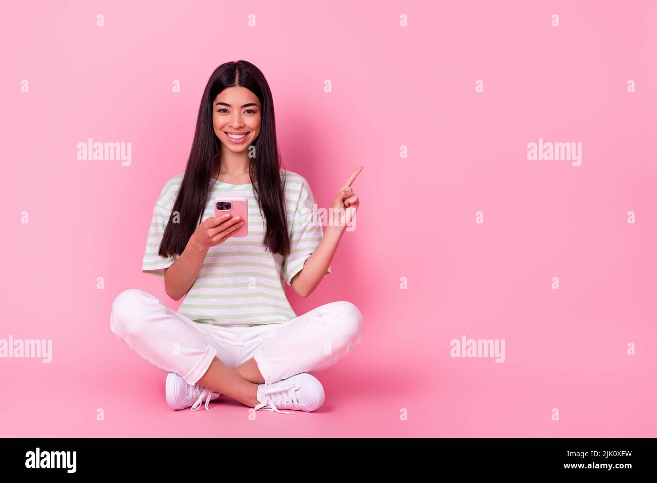 Full Length Portrait Of Positive Nice Person Sit Floor Use Telephone Indicate Finger Empty Space