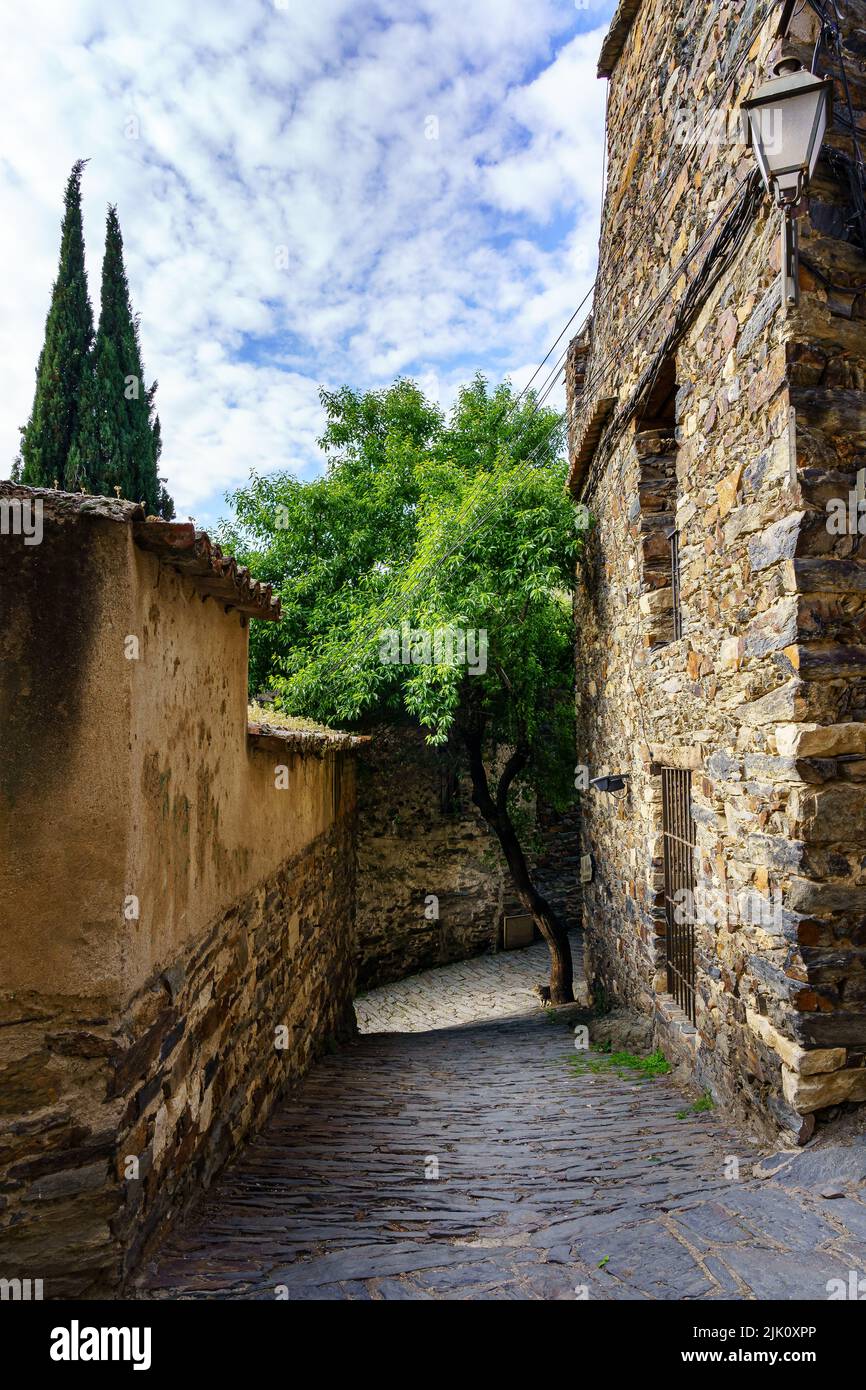 Narrow alley with old stone houses and blue sky with clouds, cypress ...