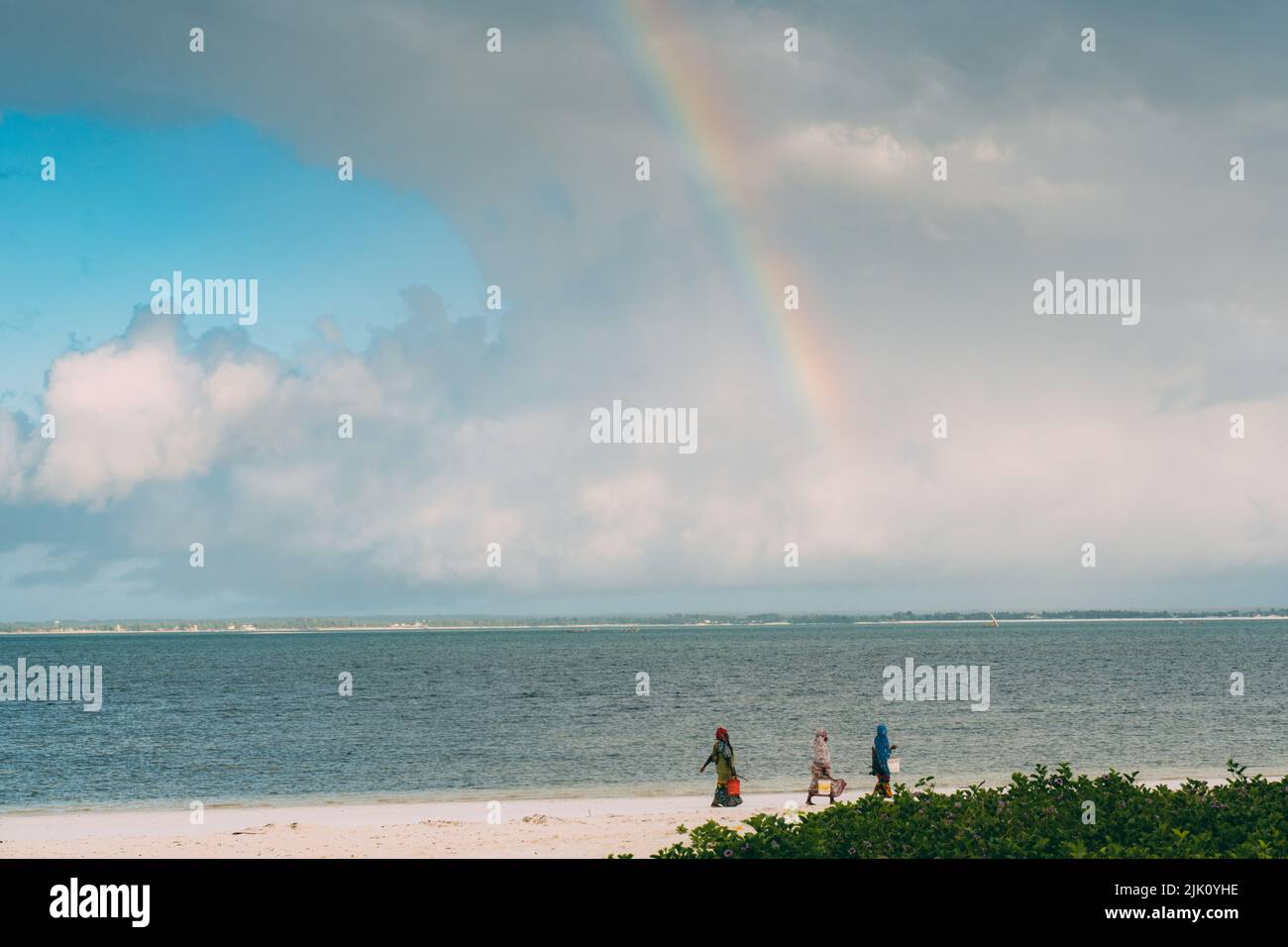 Three women walking on a white sand beach under a cloudy sky with a ...