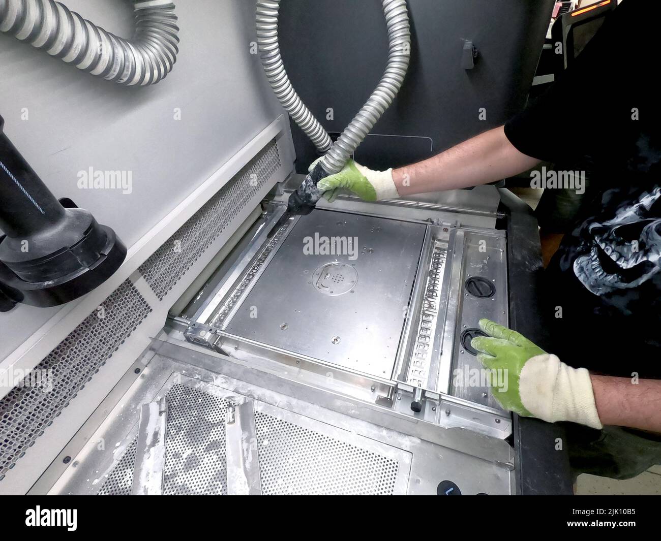 A male worker cleans the surface of an industrial 3D printer from white ...
