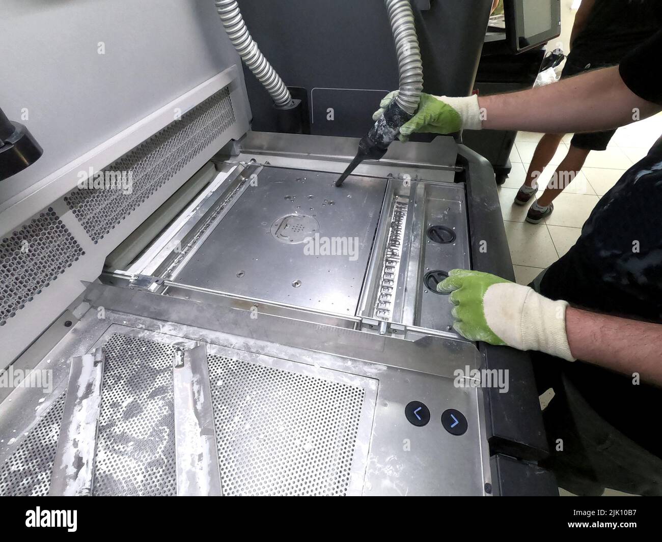 A male worker cleans the surface of an industrial 3D printer from white ...