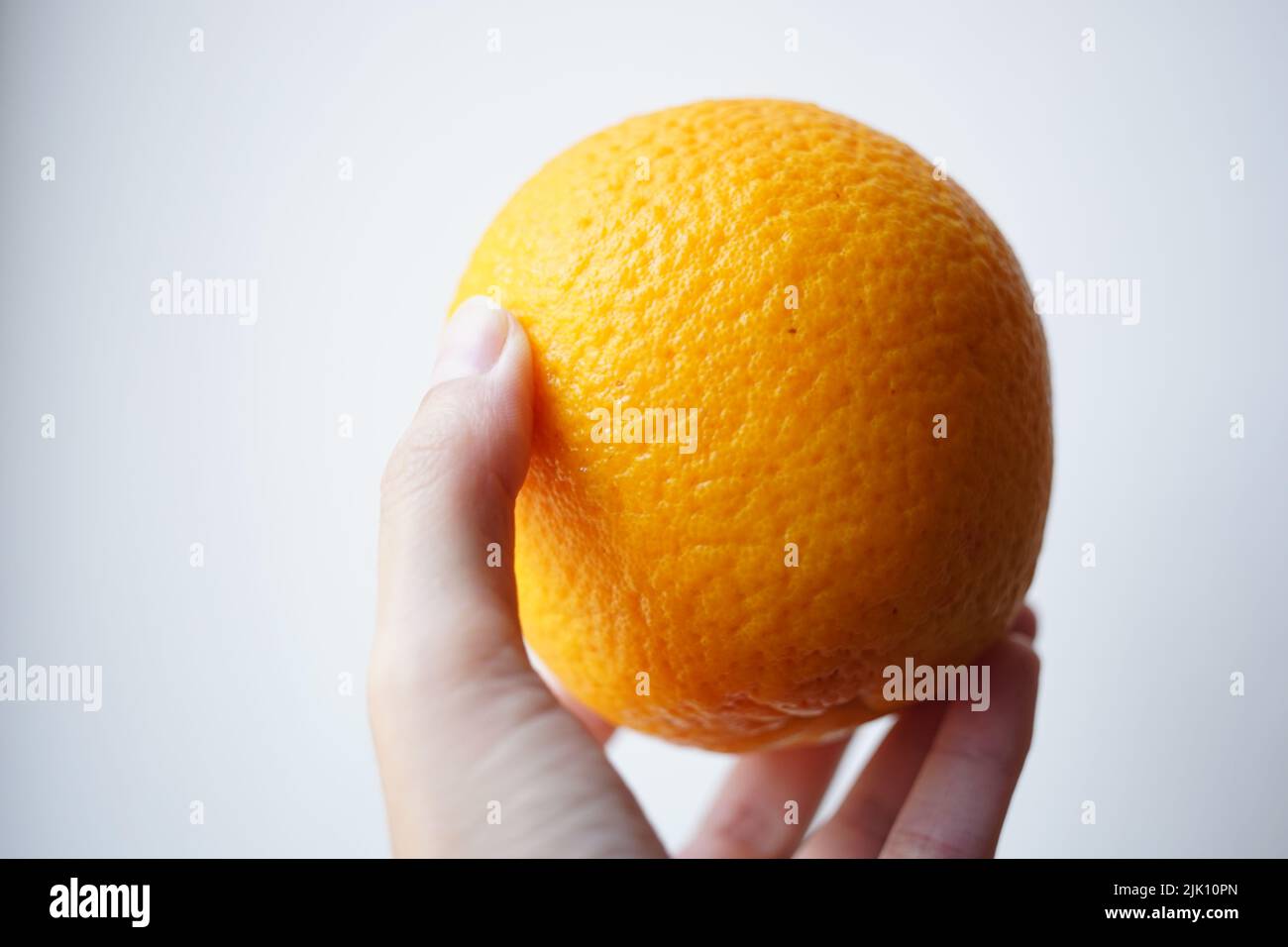 Ripe orange in female fingers on white background Stock Photo - Alamy