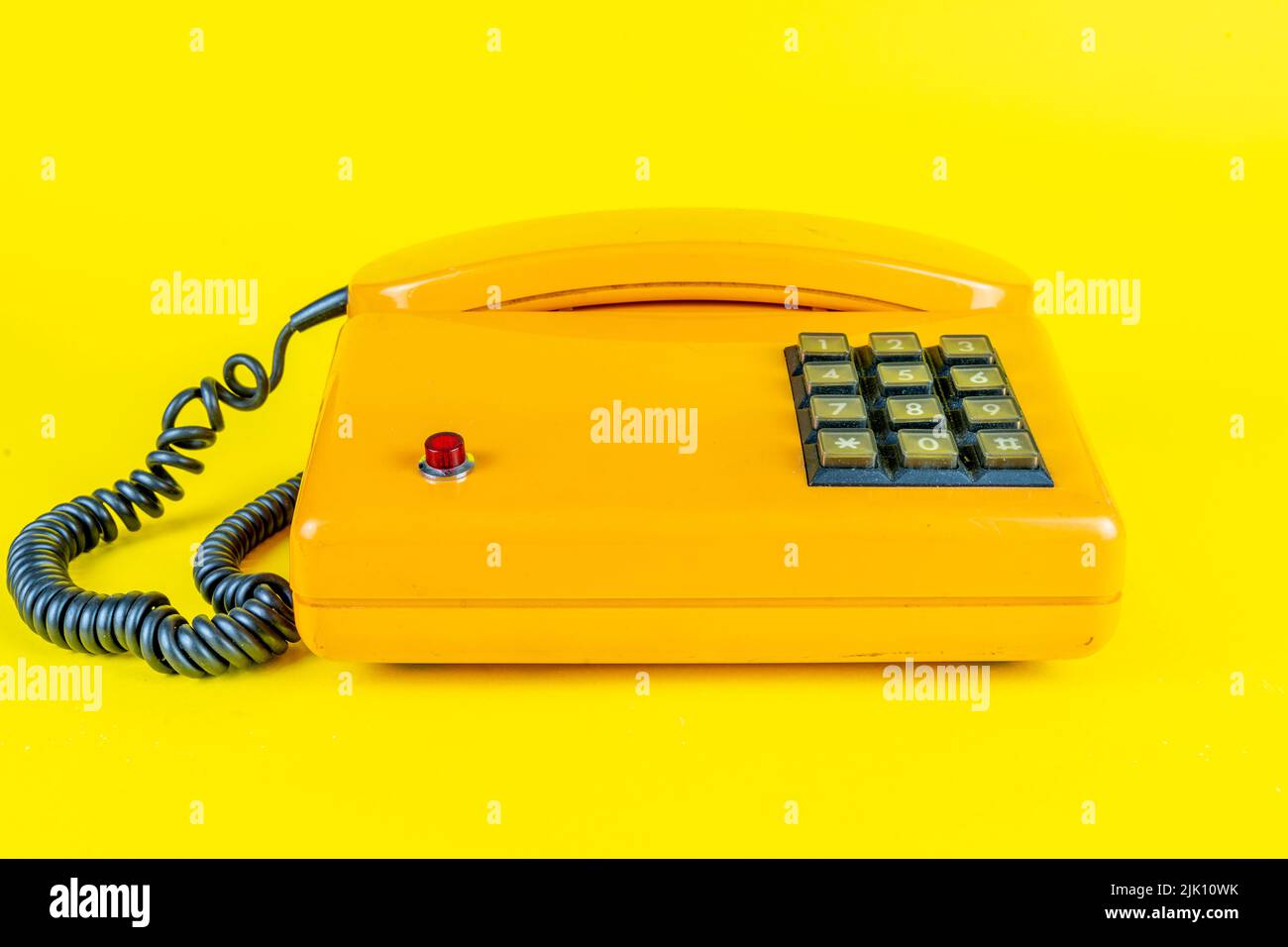 yellow plastic vintage telephone with red button on a yellow background ...
