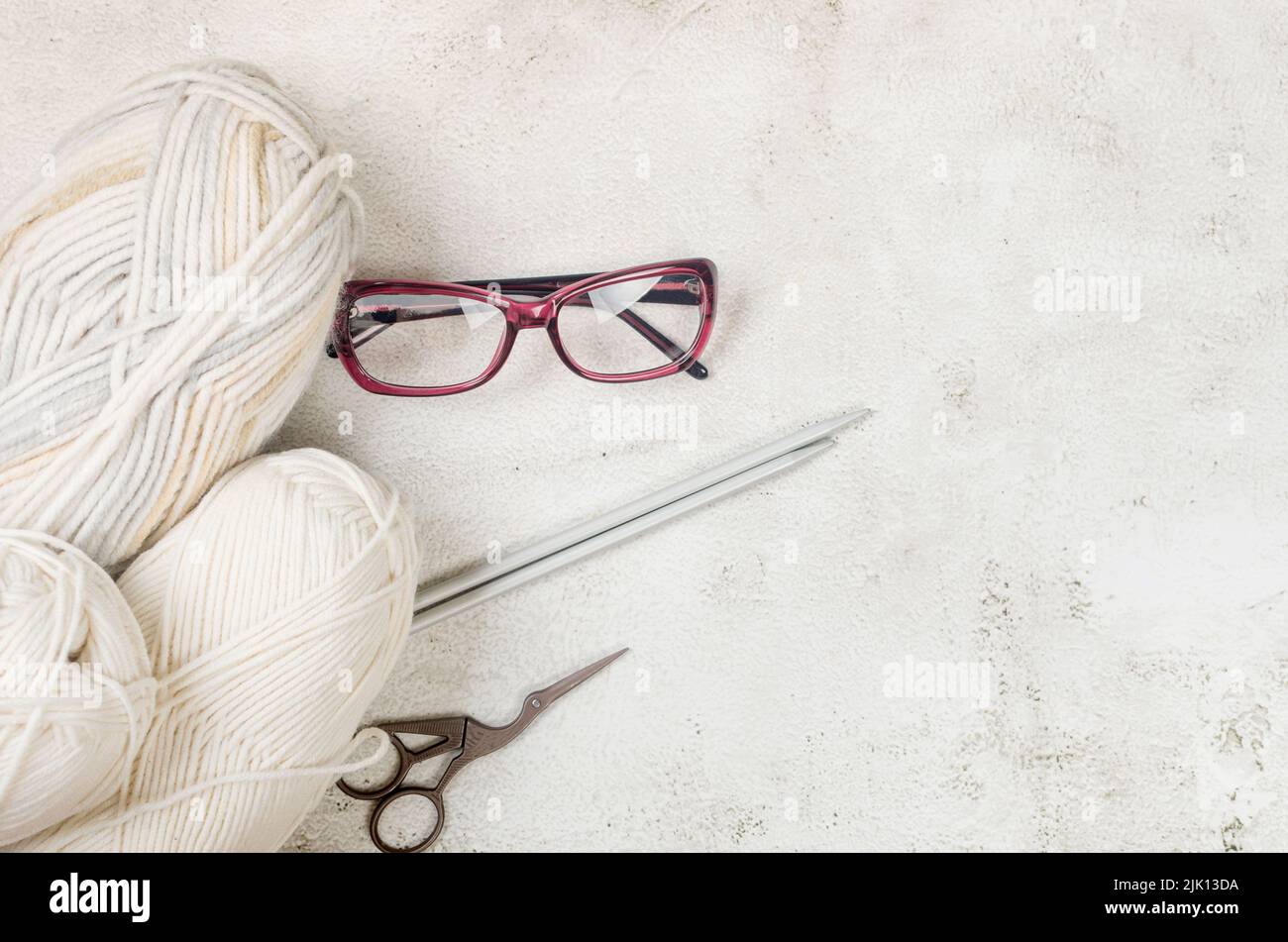 Light beige knitting wool, knitting needles and eyeglesses on conkrete ...