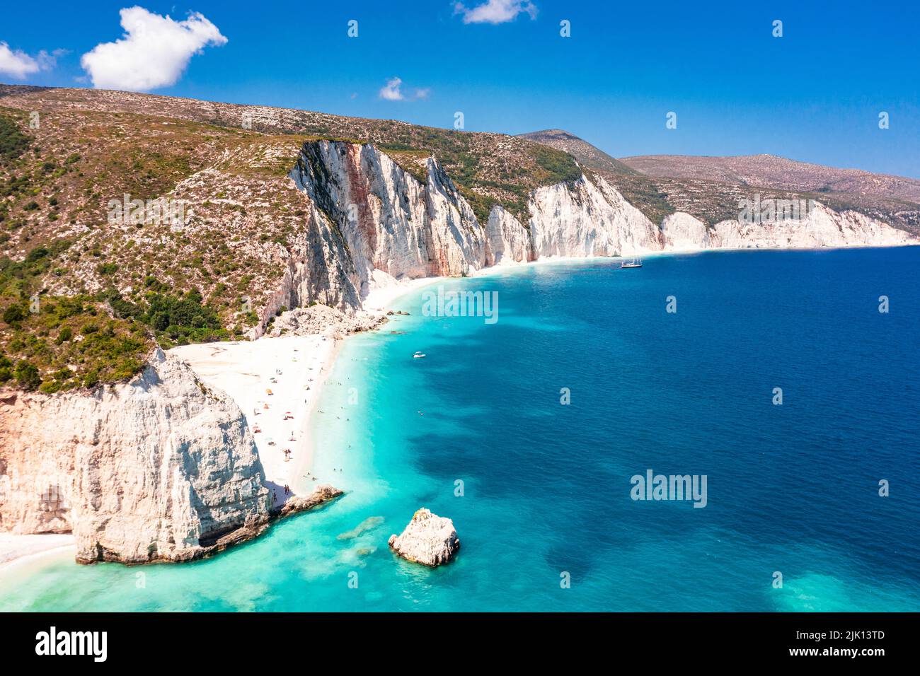 Tourists sunbathing at idyllic Fteri Beach set among cliffs and blue ...