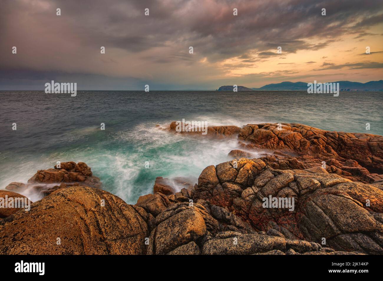A scenic view of a beautiful seascape with rocks in a colorful sunset ...