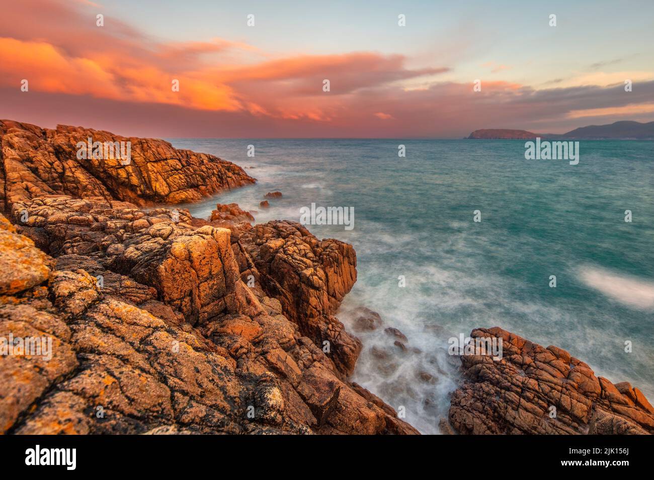 A scenic view of a beautiful seascape with rocks in a colorful sunset ...