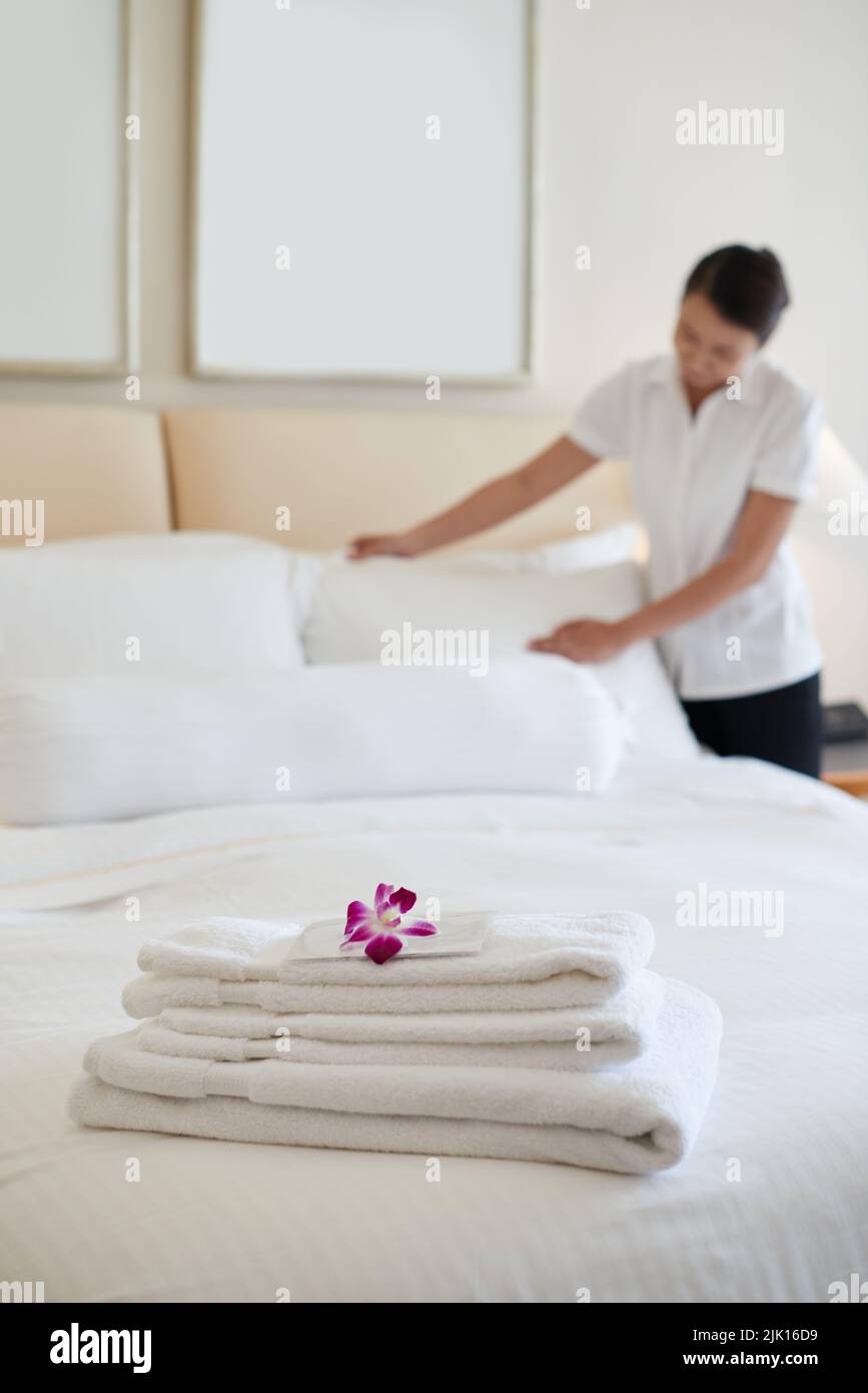 Maid making bed for the guests, focus on stack of towels Stock Photo ...