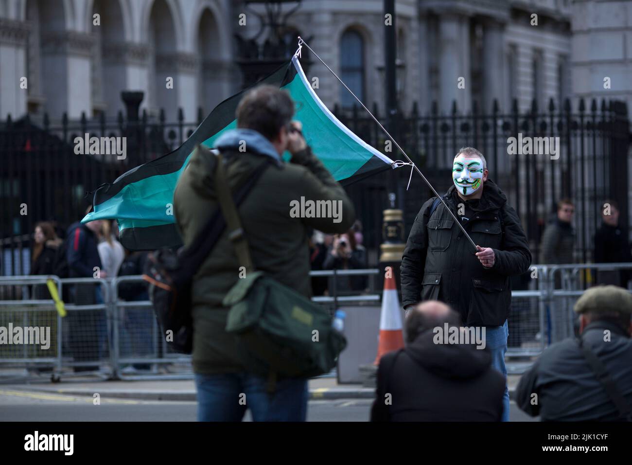 A person wearing a mask is surrounded by photographers during a Cost of ...