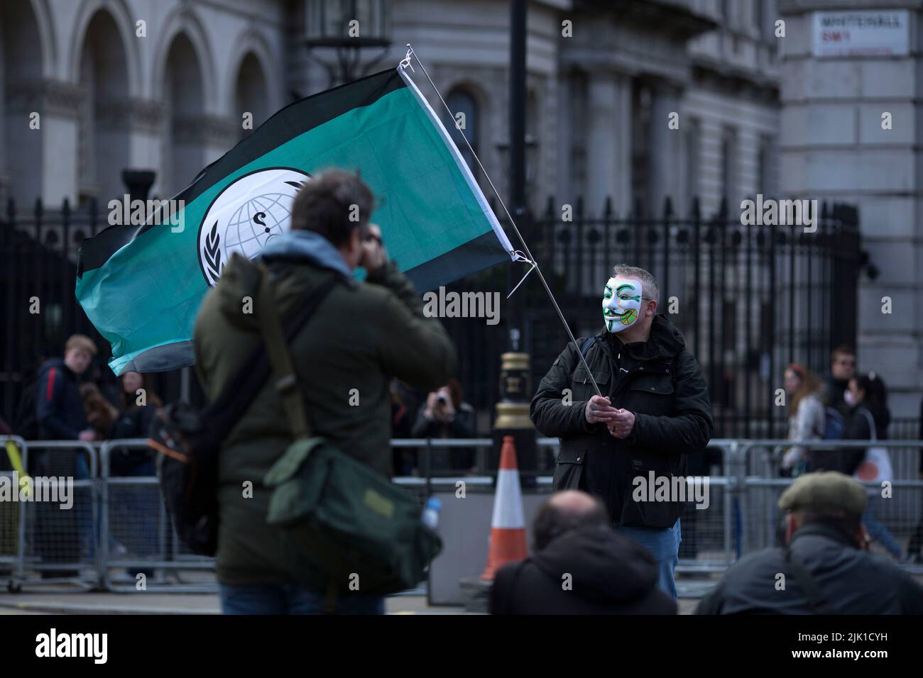 A person wearing a mask is surrounded by photographers during a Cost of ...