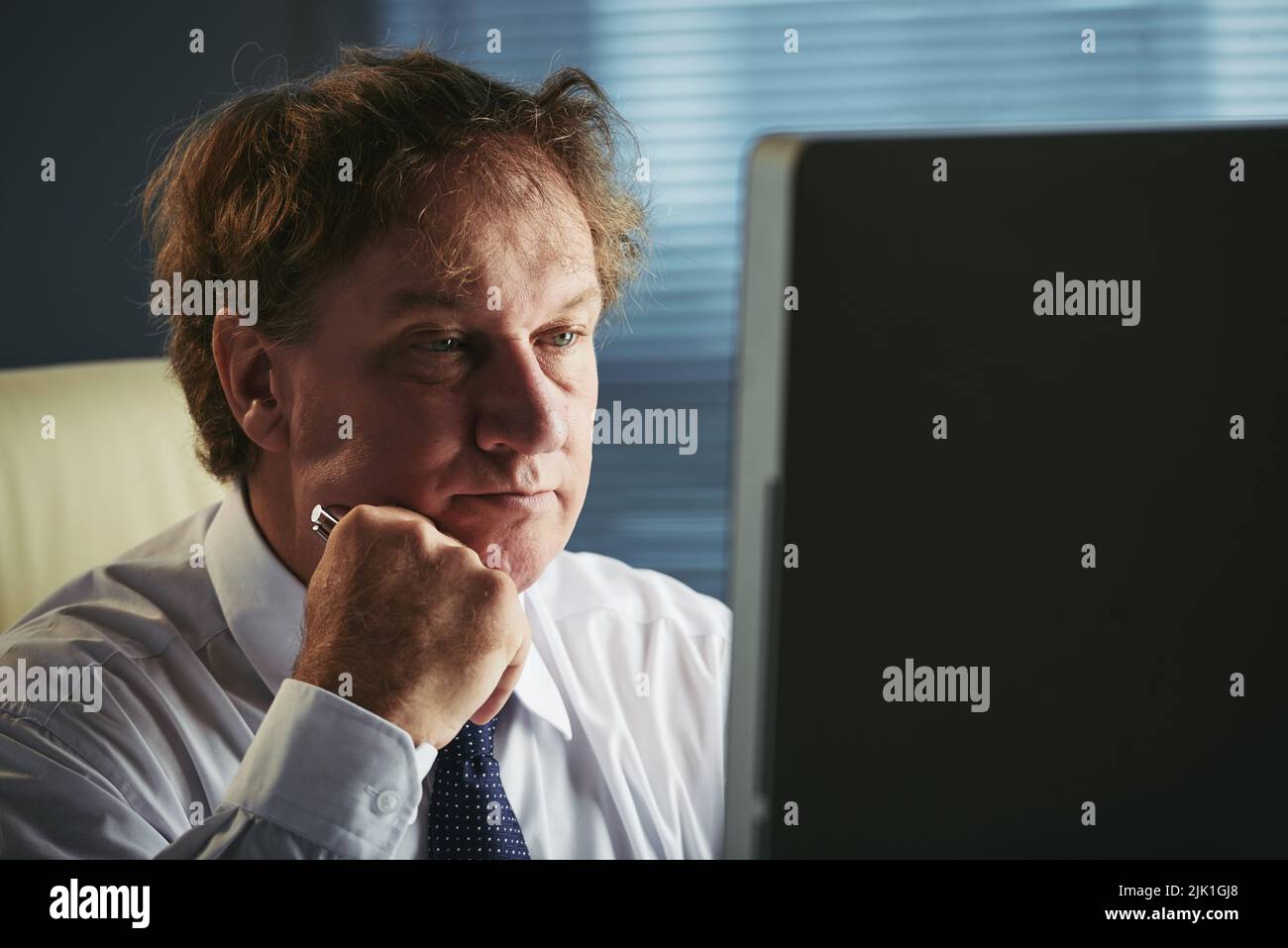 Pensive businessman reading articles on his computer screen in his ...