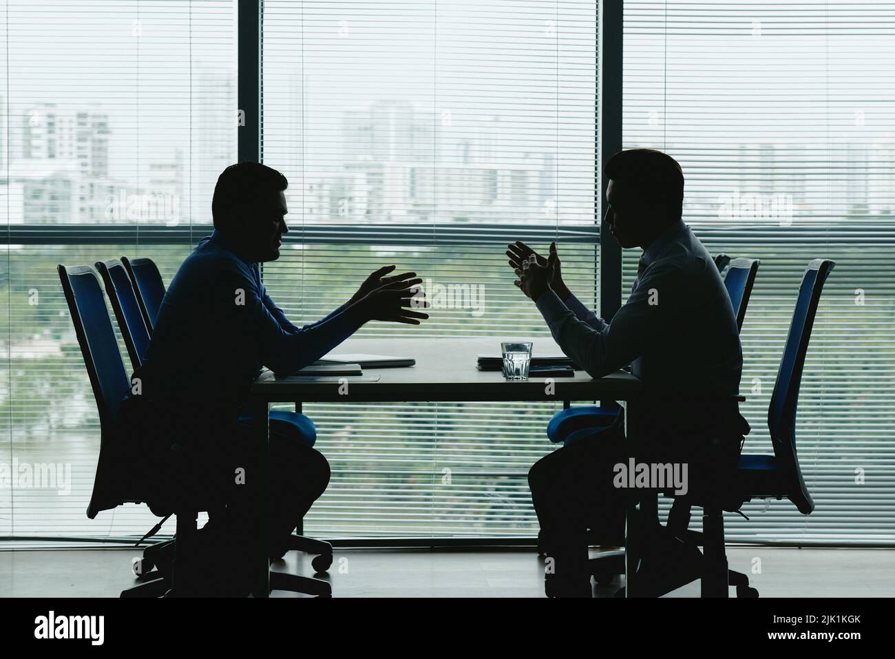 Silhouettes of business people sitting at table against the office ...