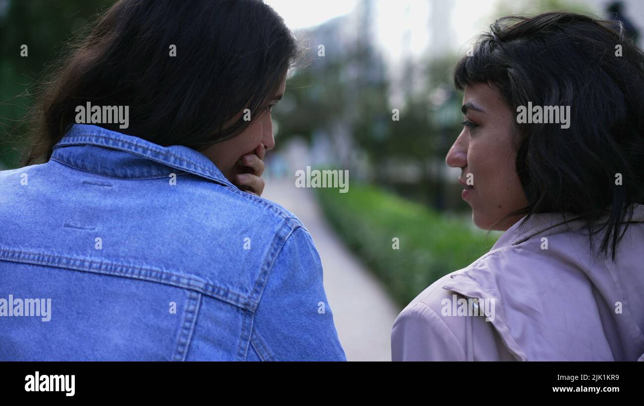 Female friends gossiping outside while walking together. Back of two ...