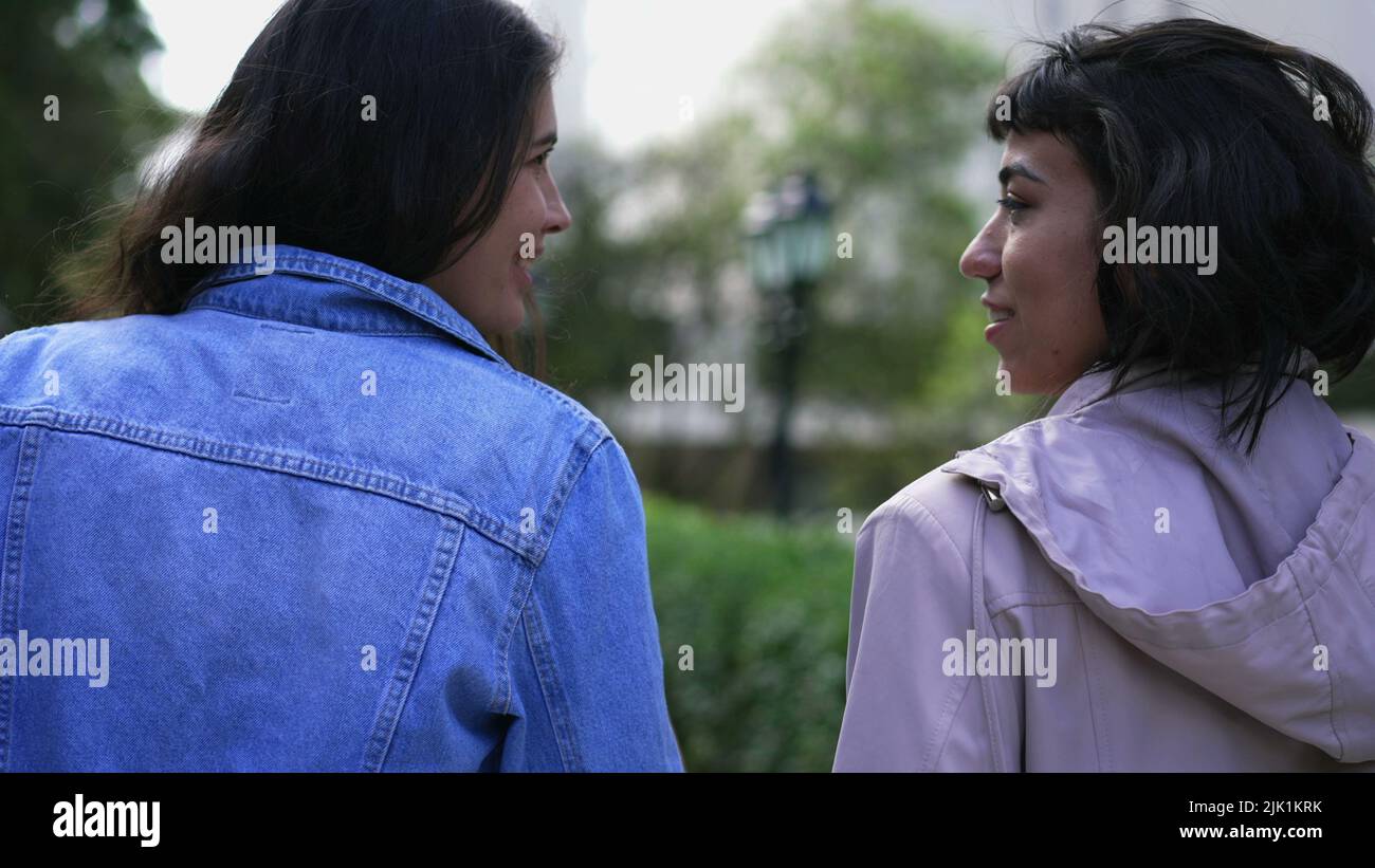 Female friends gossiping outside while walking together. Back of two ...