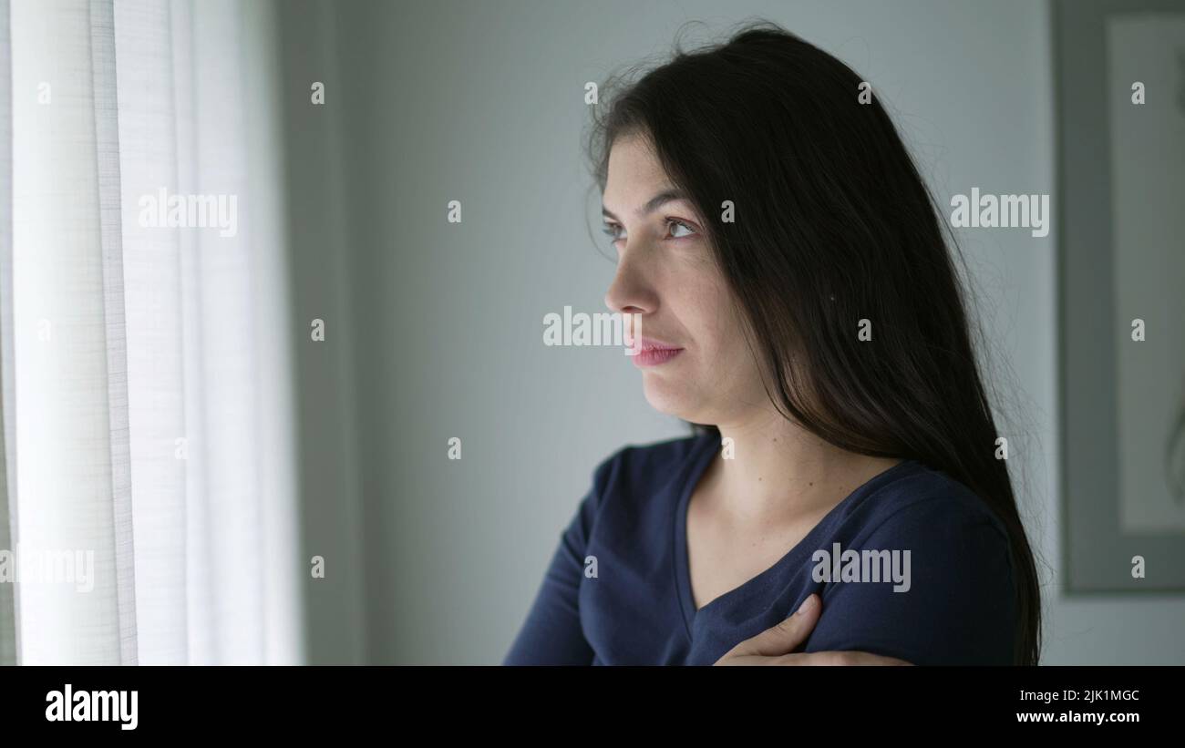 Anxious young woman trying to calm herself standing by window looking ...