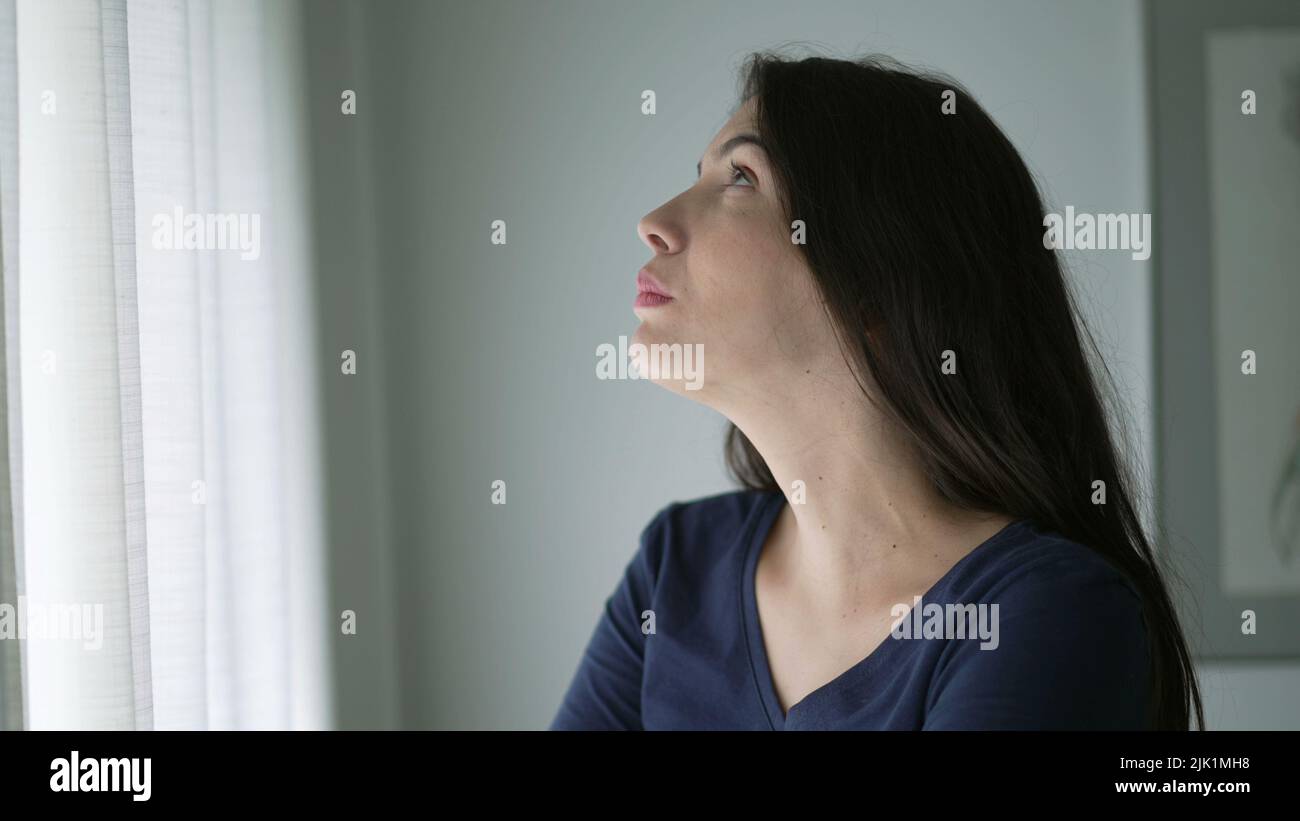Anxious young woman trying to calm herself standing by window looking ...