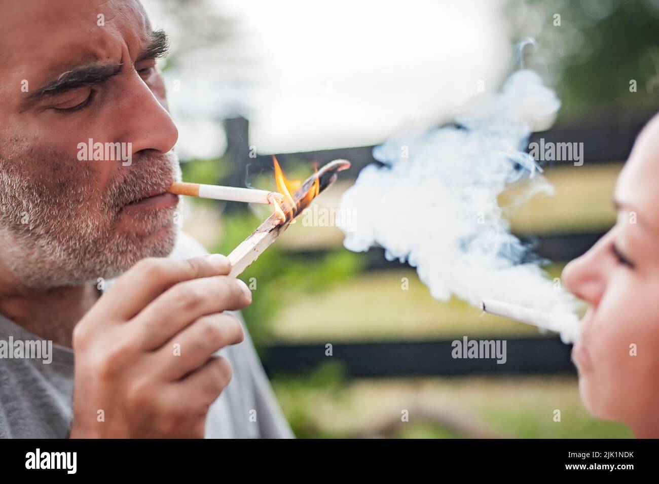 A man and a woman smoke cigarettes together, a man lights a cigarette ...