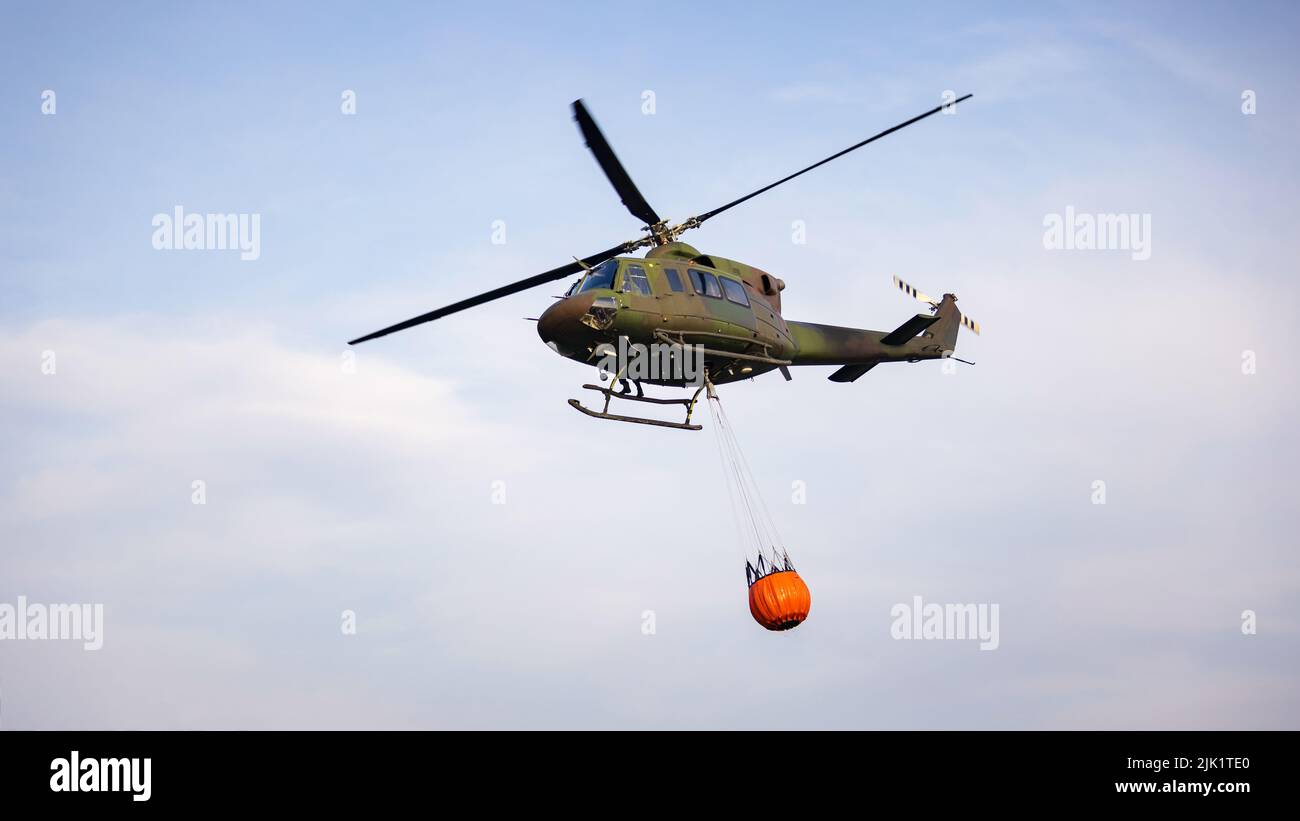 Wildfire firefighting in forest with helicopter carrying a water bucket ...