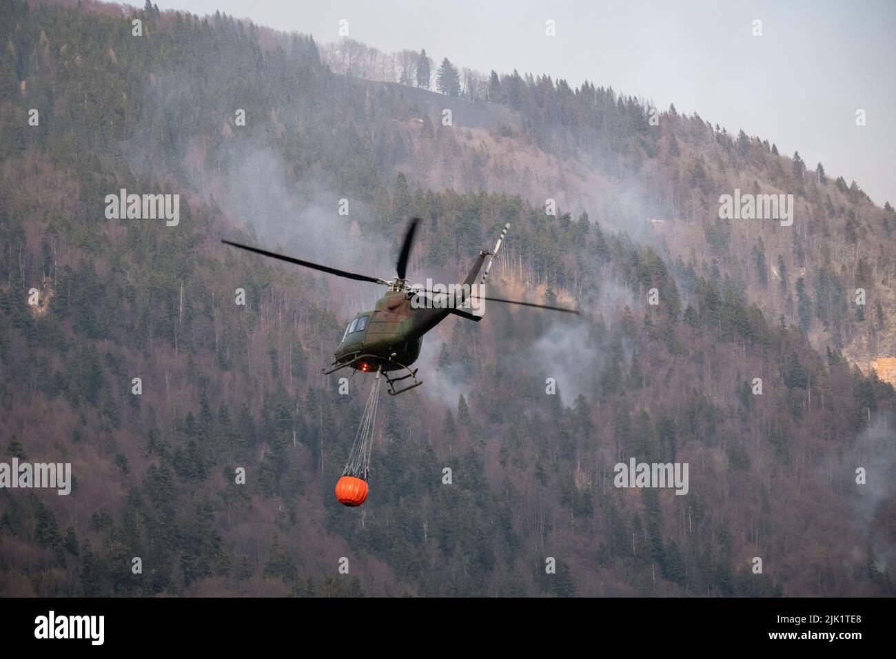 Wildfire firefighting in forest with helicopter carrying a water bucket ...