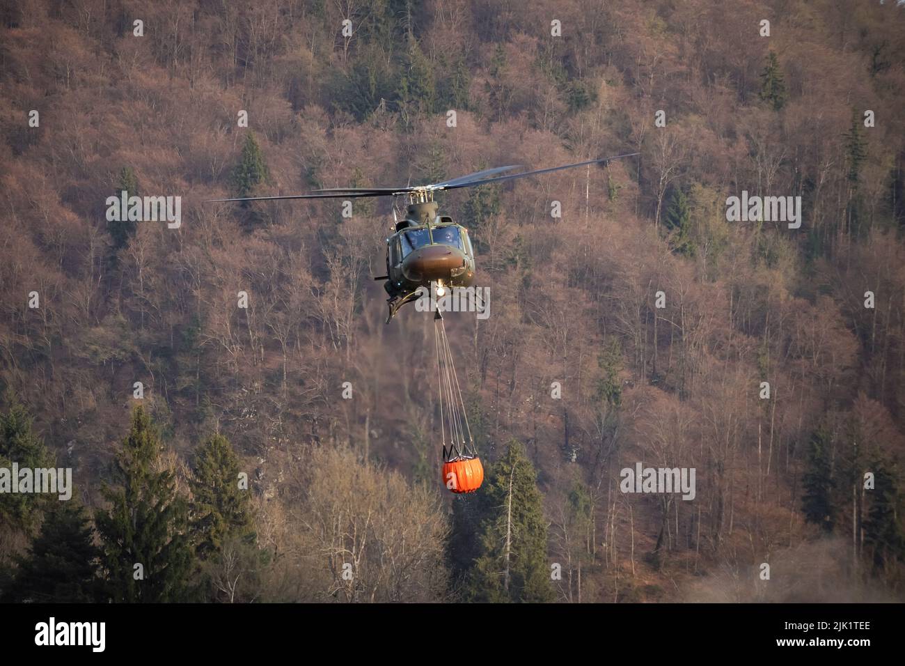 Wildfire firefighting in forest with helicopter carrying a water bucket ...